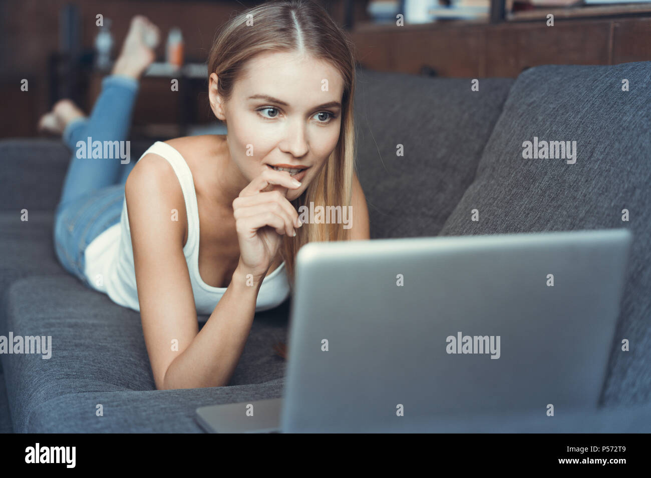 Casual young woman lying on couch and using laptop at home Stock Photo ...