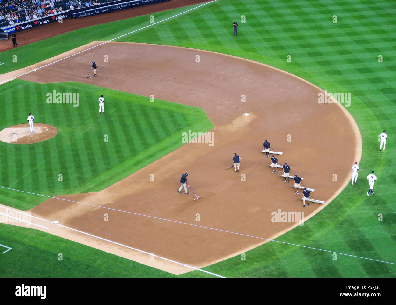 The grounds crew groom the infield dirt between innings during a night ...