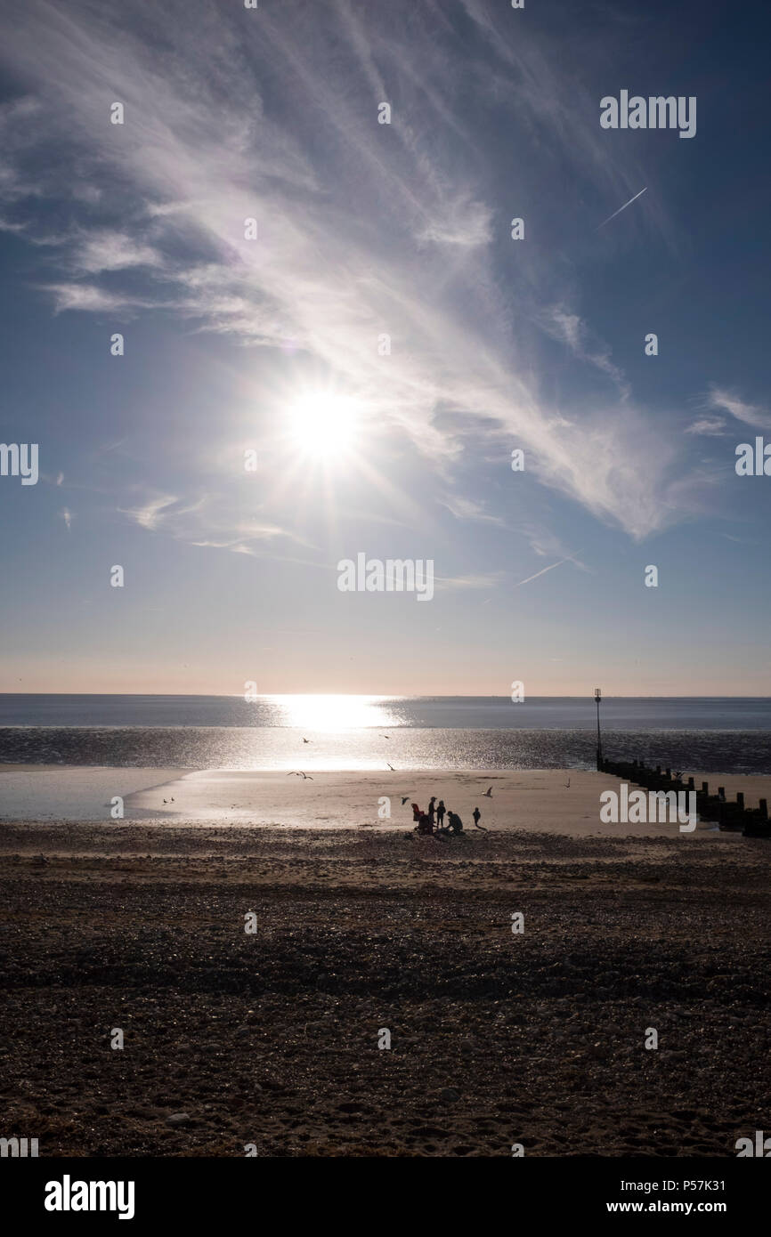 Sun setting over a beach with distant figures silhouetted Stock Photo ...