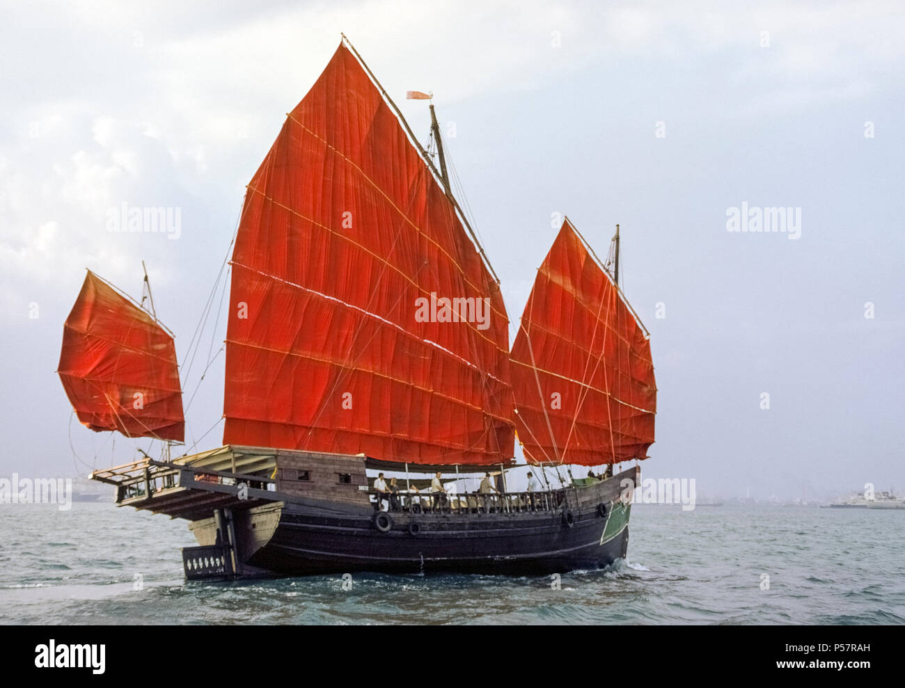 A wooden Chinese junk with traditional red sails catches the wind that ...