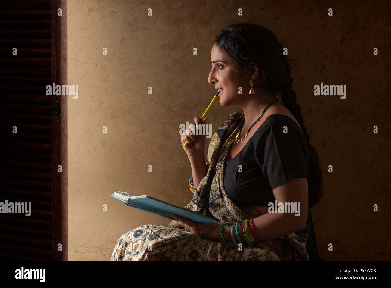 Indian rural woman thinking while holding book and pencil Stock Photo ...