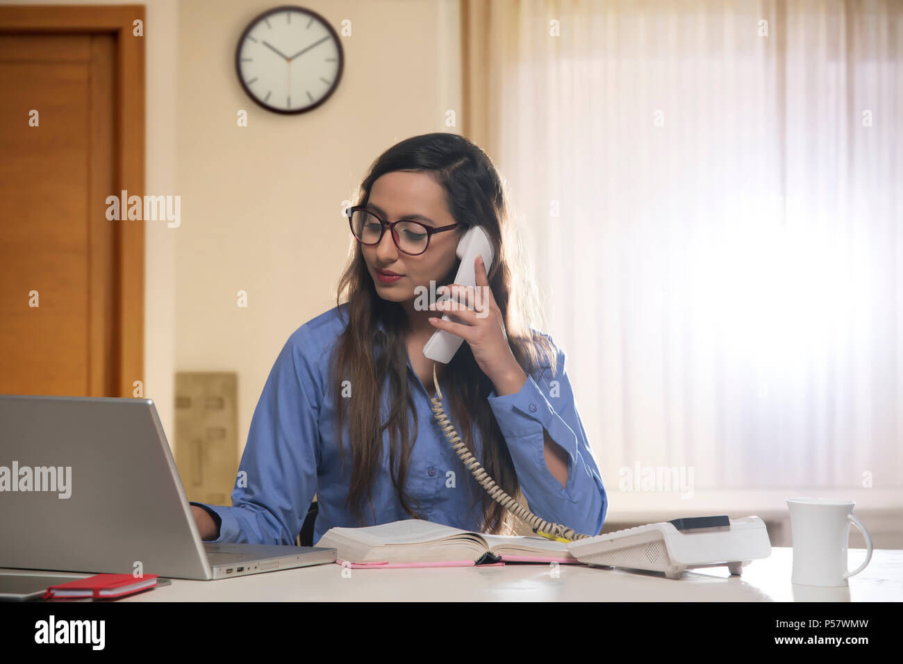 Young female office worker using telephone and laptop computer Stock ...
