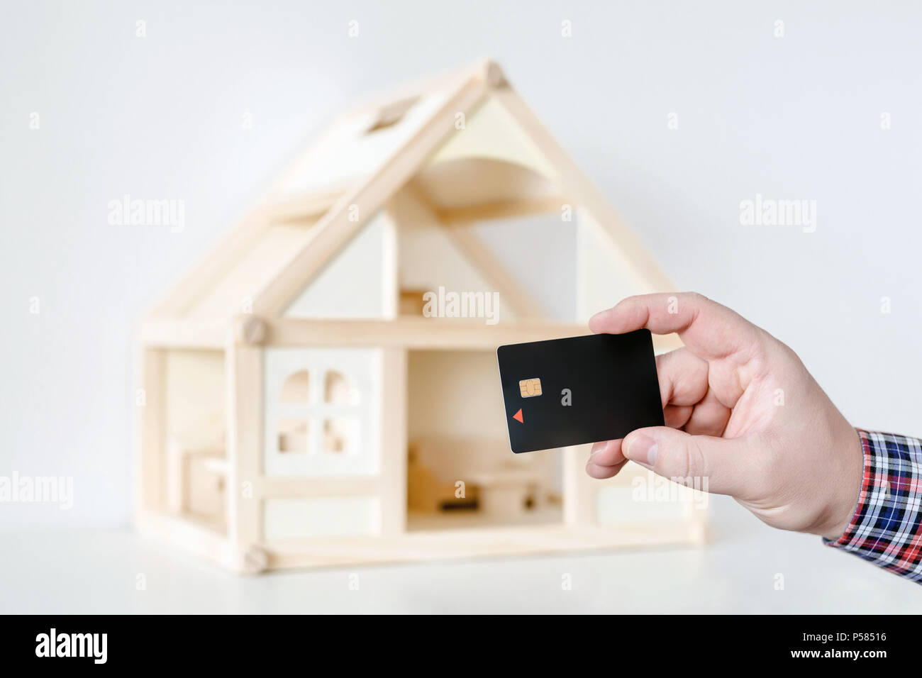 Hand holding black plastic chip card. Wooden house model on background ...