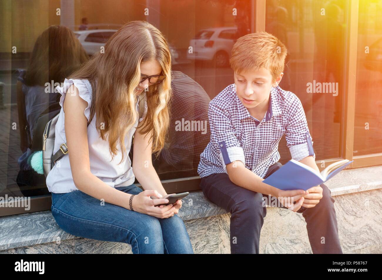 Outdoor portrait children teenagers, reading book and using smartphone ...