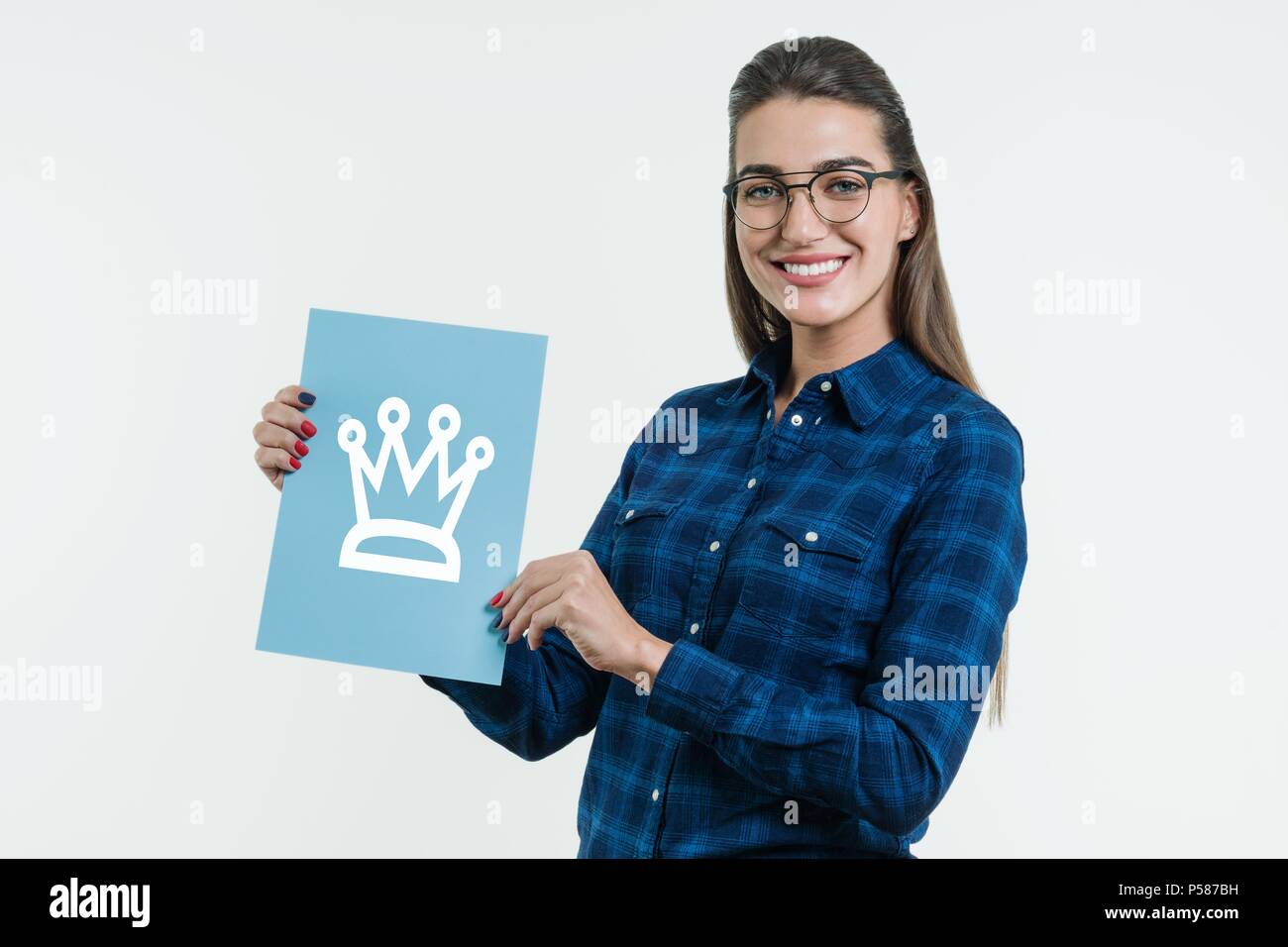 Positive young woman showing a crown sign on blue paper. White studio ...