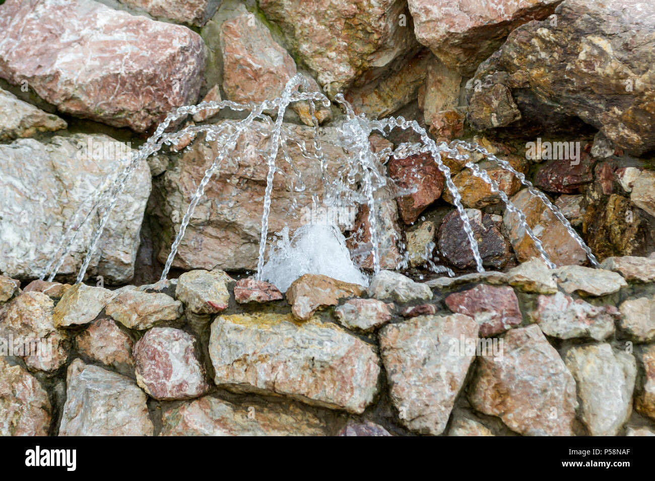 A small waterfall sprinkles drops of water down from a stone in the ...