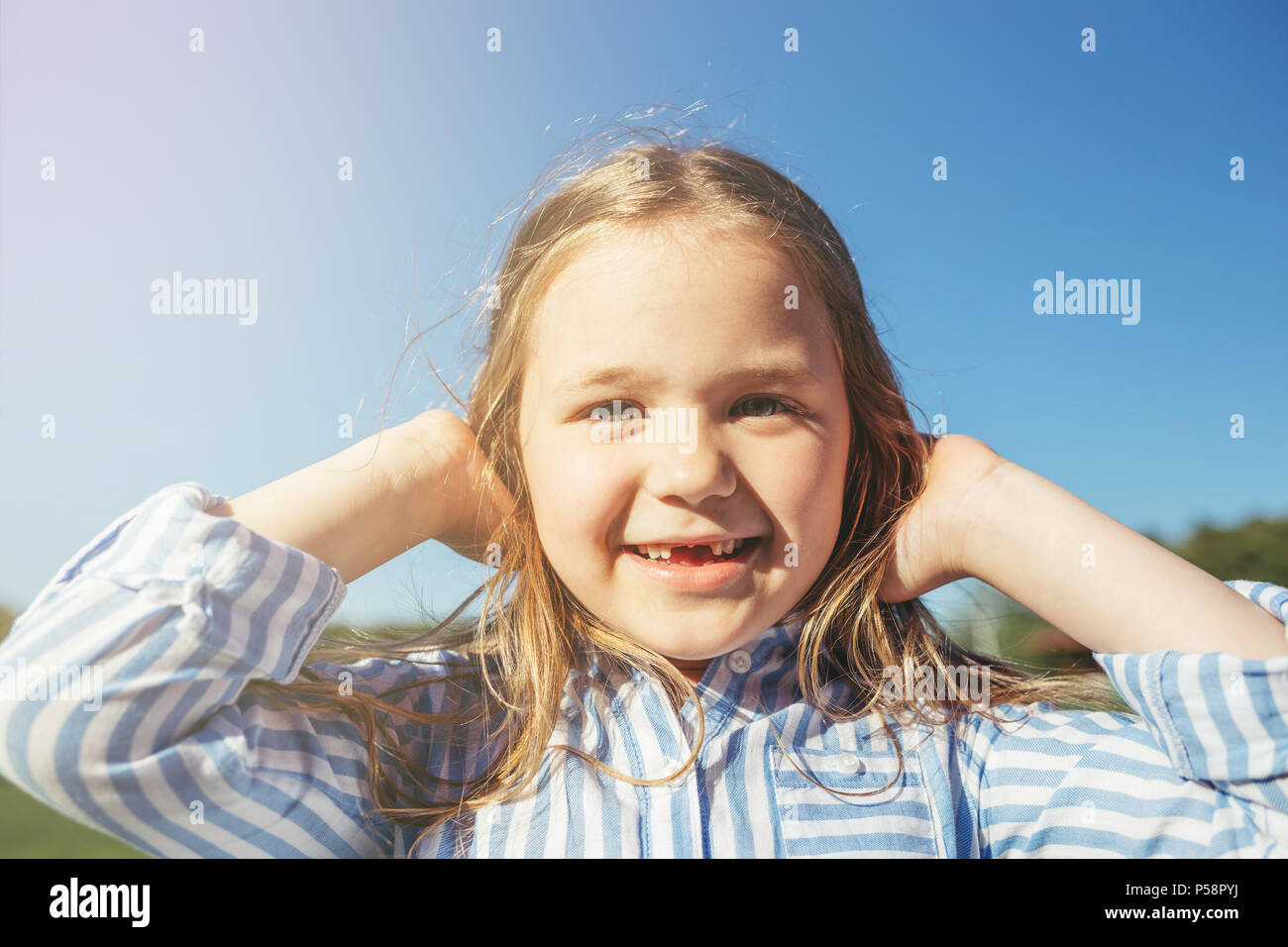 Little girl looking at camera, smiling and holding her head. Summer ...