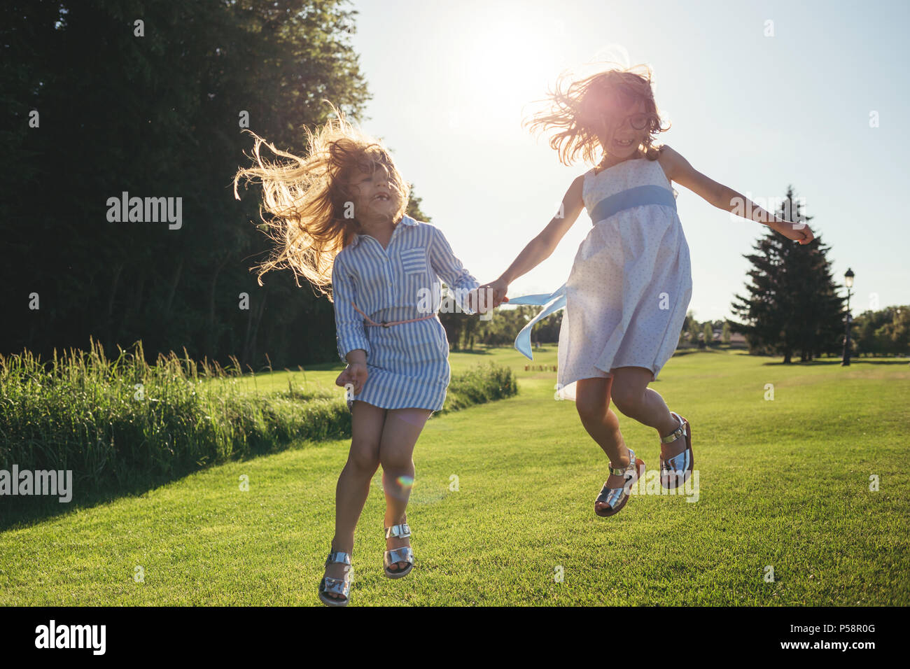 Two cheerful girls jumping against the sunset. Summer activity and ...