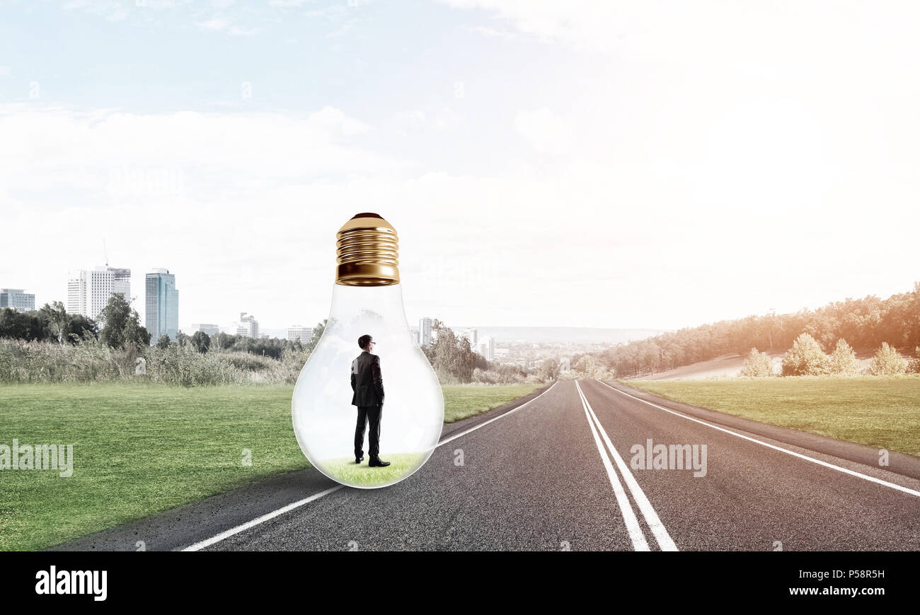 Young businessman trapped inside of light bulb on asphalt road Stock ...