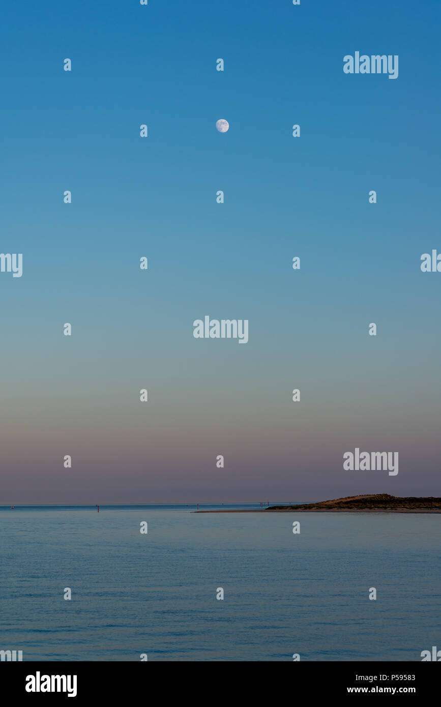Moon high in the sky at dusk above the sea off the coast of Dorset in ...
