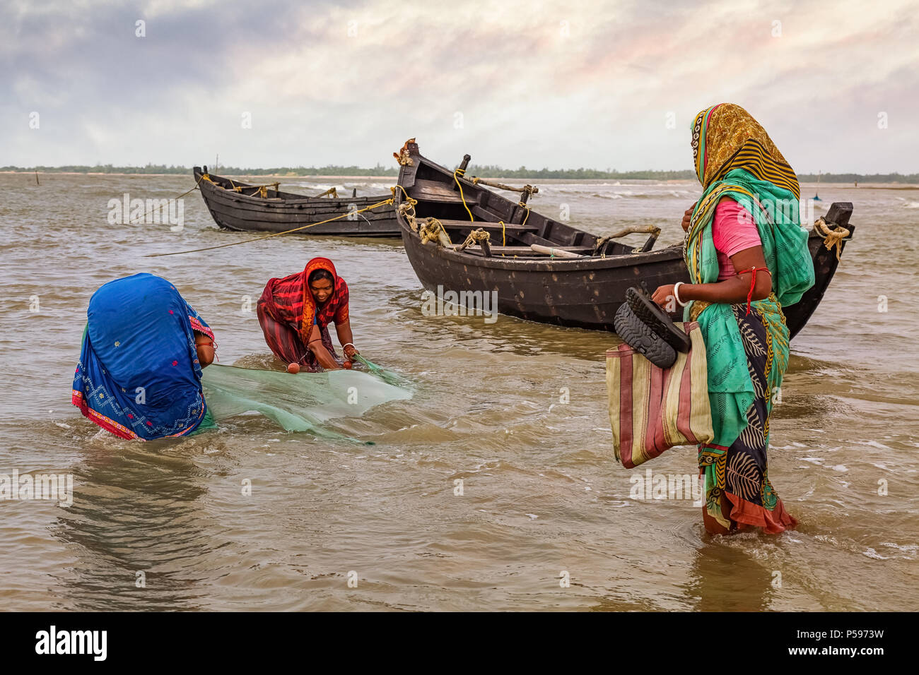 Rural women fishing with nets at sea with view of wooden fishing boats ...