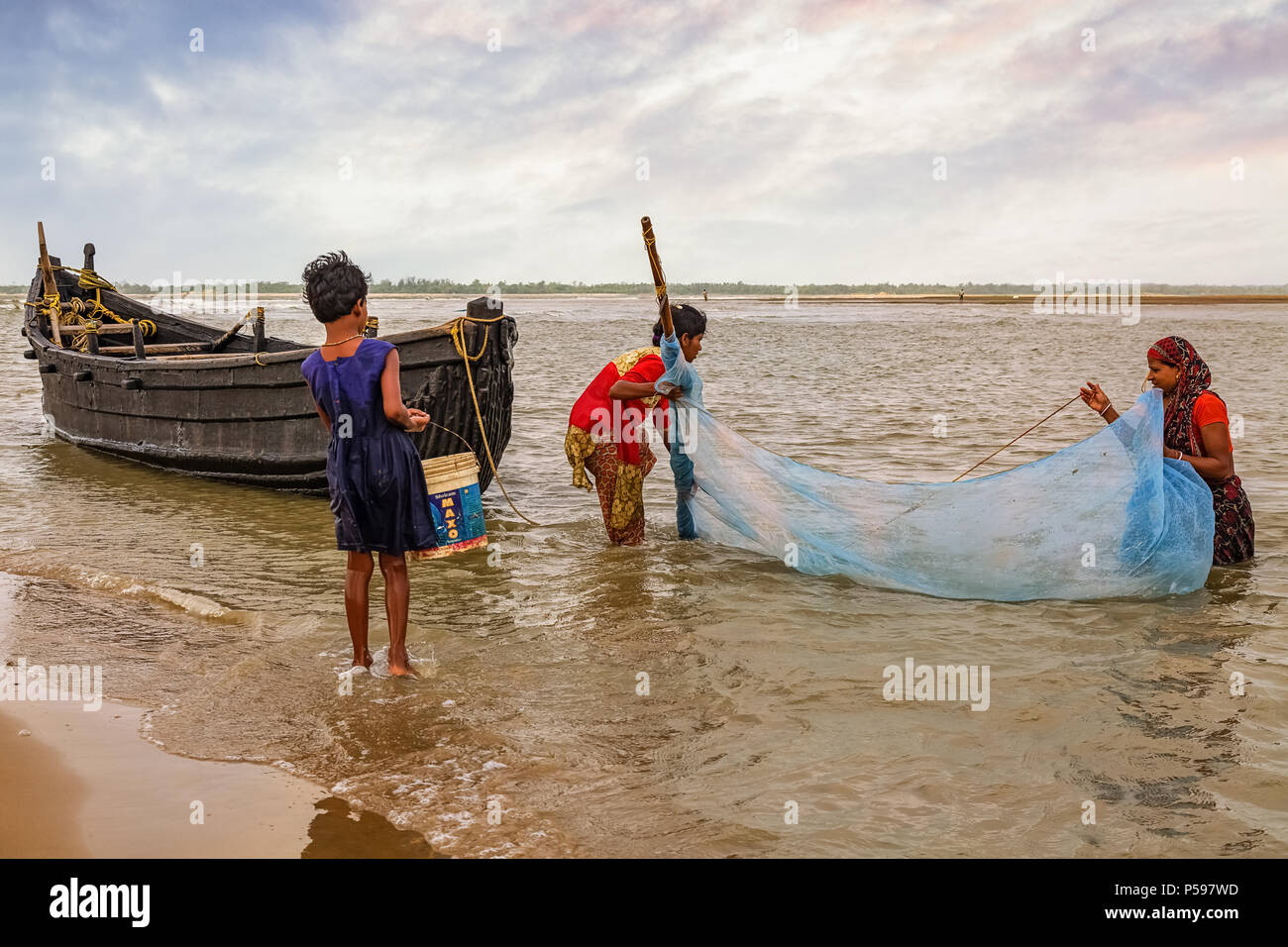 Rural women fishing with nets at sea with view of wooden fishing boats ...