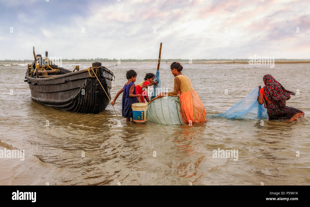 Rural women fishing with nets at sea with view of wooden fishing boats ...