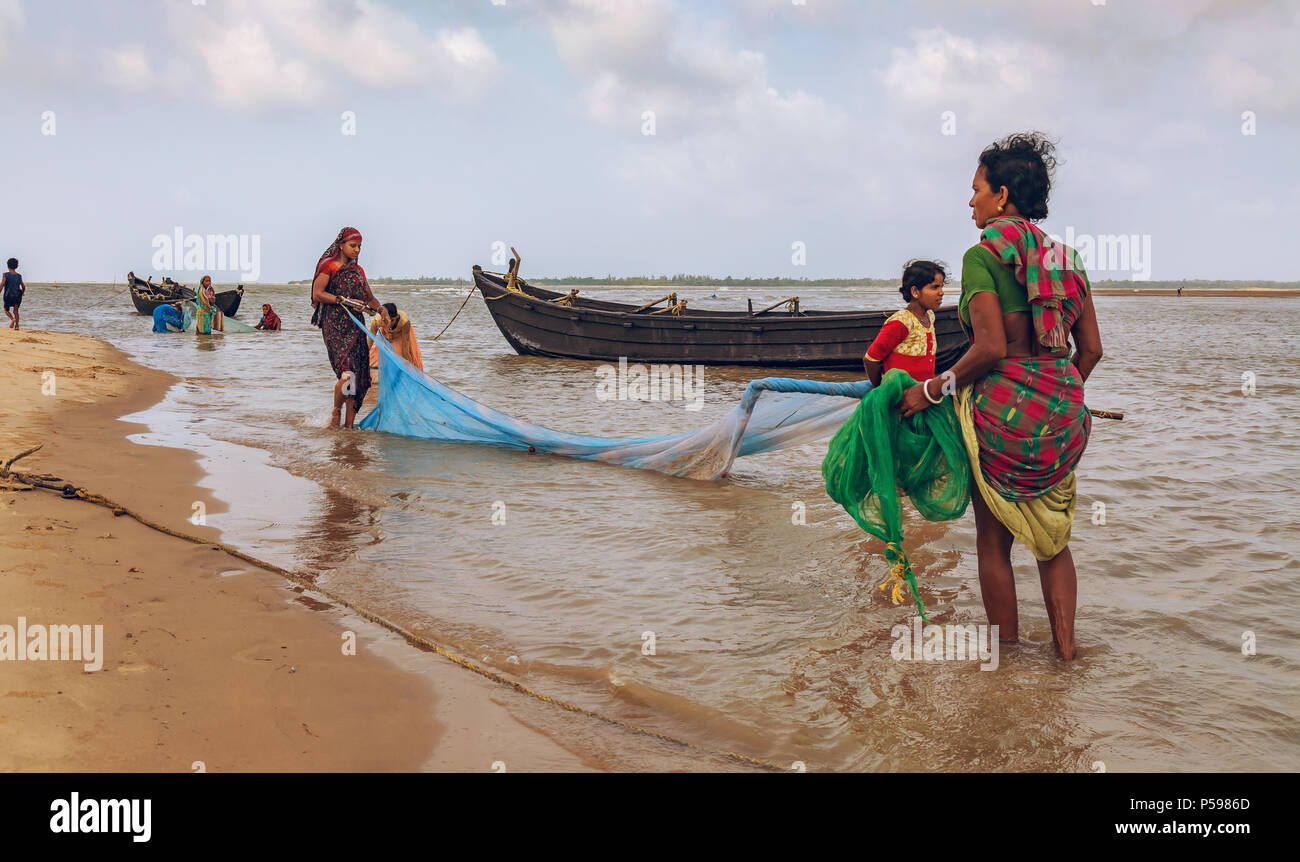 Rural women fishing with nets at sea with view of wooden fishing boats ...