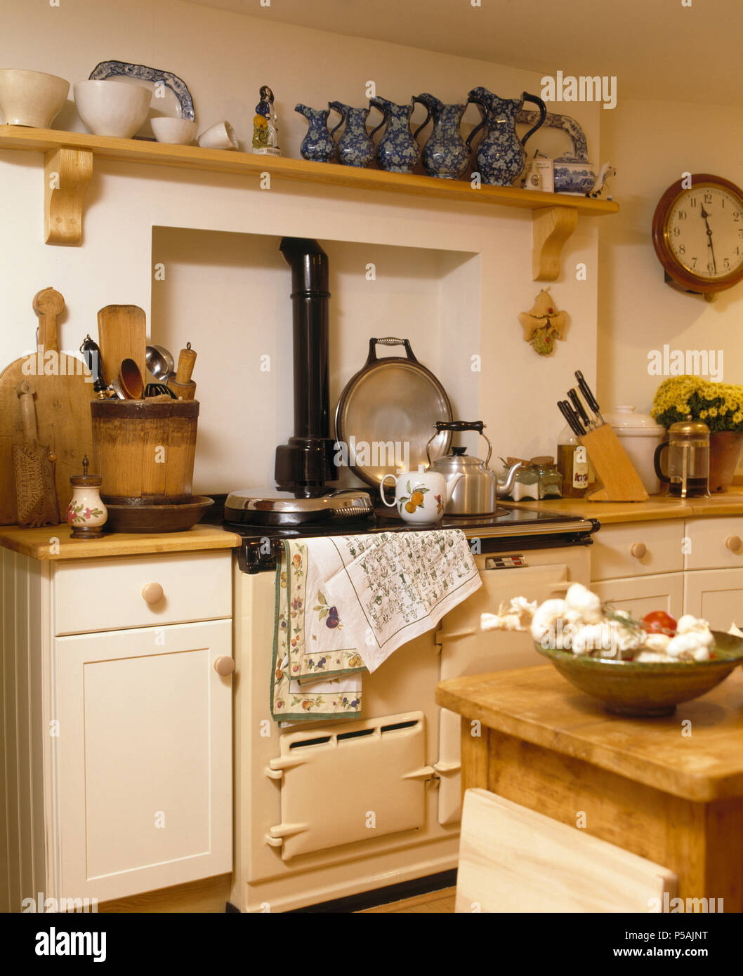 Row of blue jugs on wooden shelf above cream Aga in cottage kitchen ...