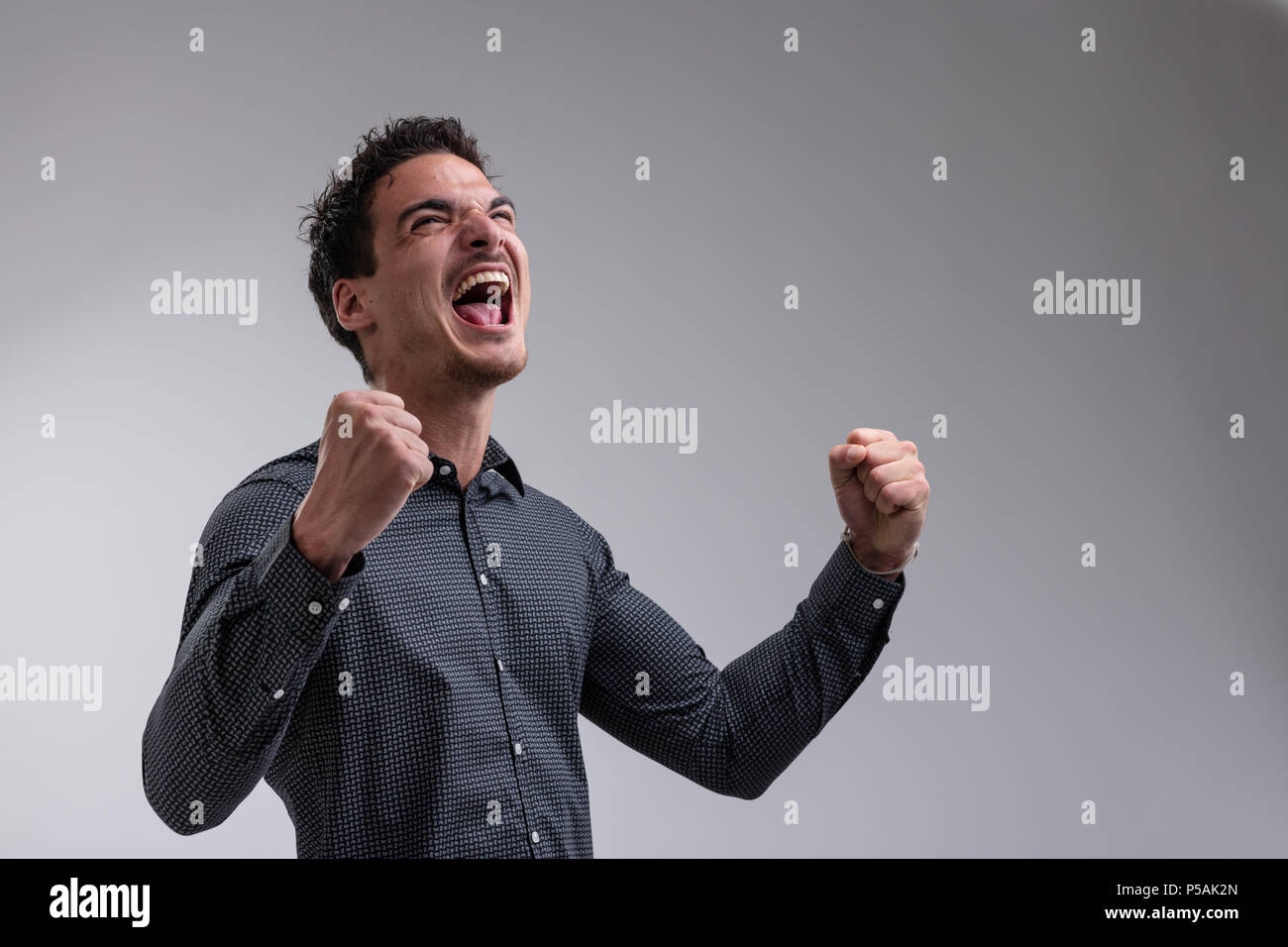 young man exulting rising his arms and hands with his mouth open and ...