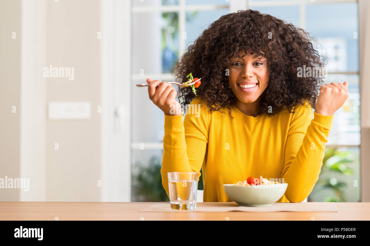 African american woman eating pasta salad at home screaming proud and ...