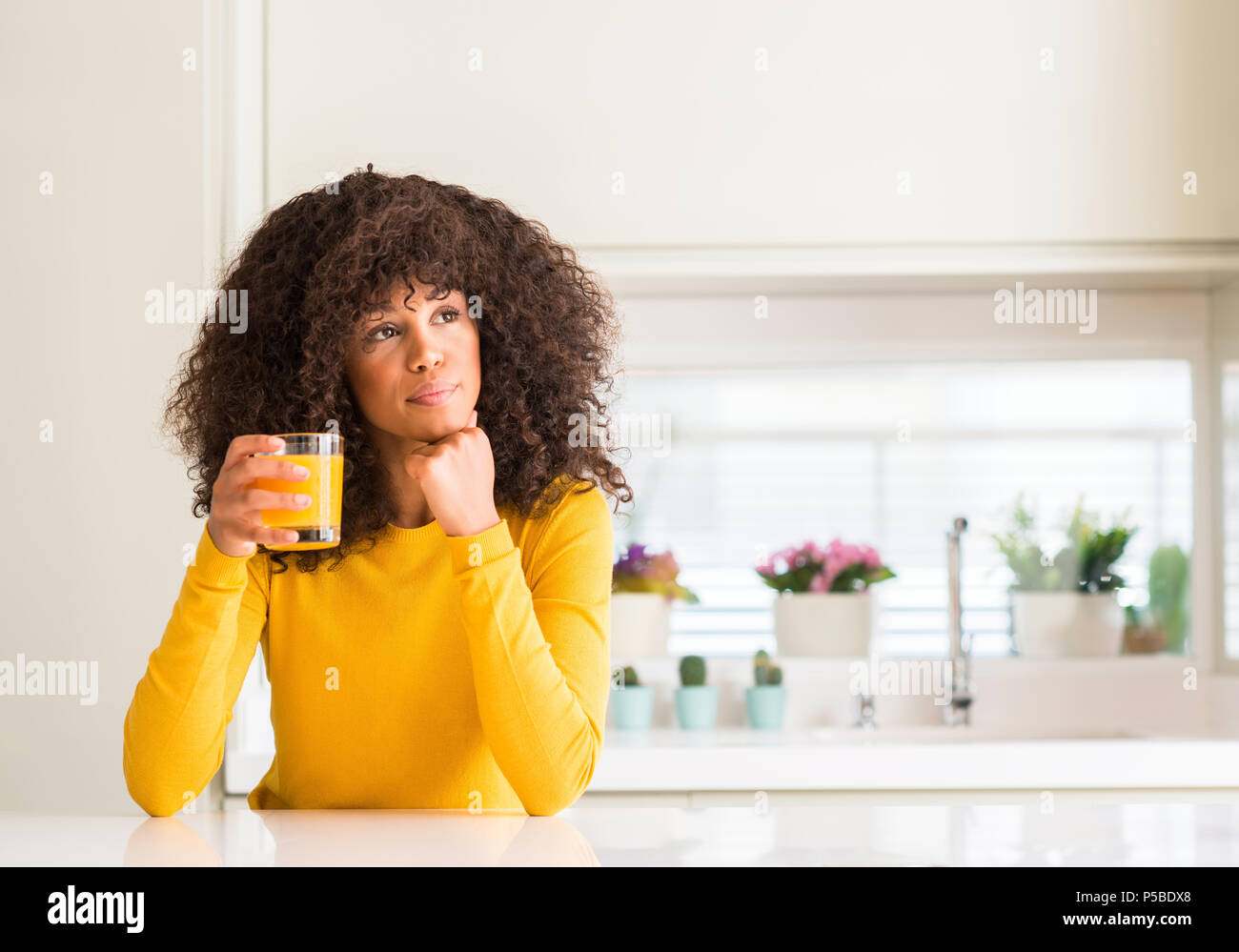 African american woman drinking orange juice in a glass serious face ...