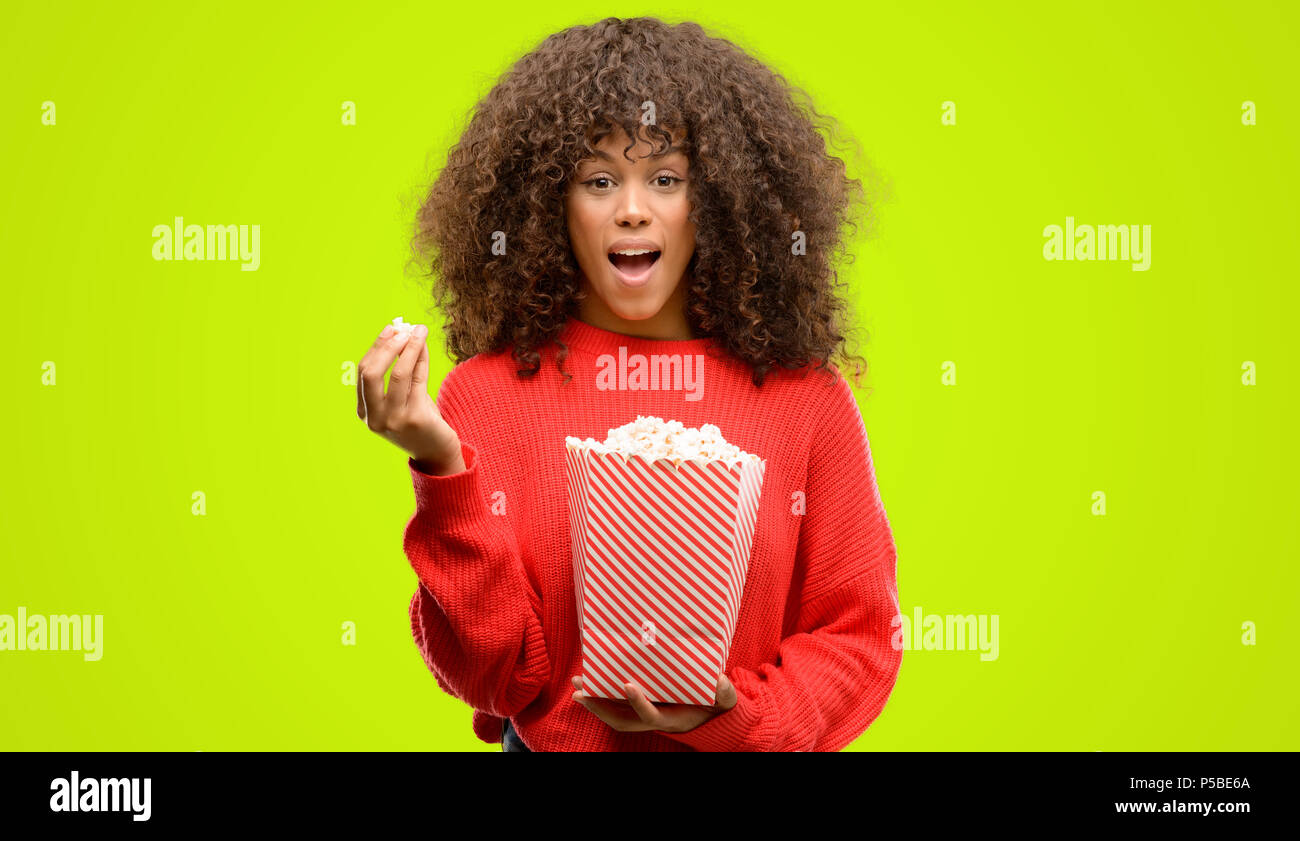 African american woman eating popcorn scared in shock with a surprise ...