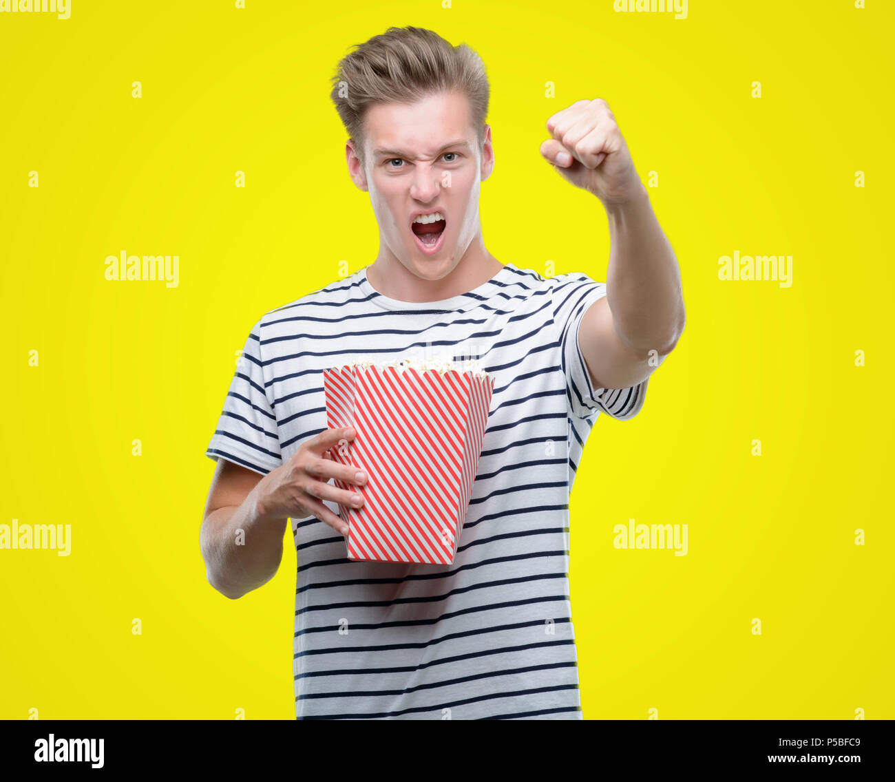 Young handsome blond man eating popcorn annoyed and frustrated shouting ...
