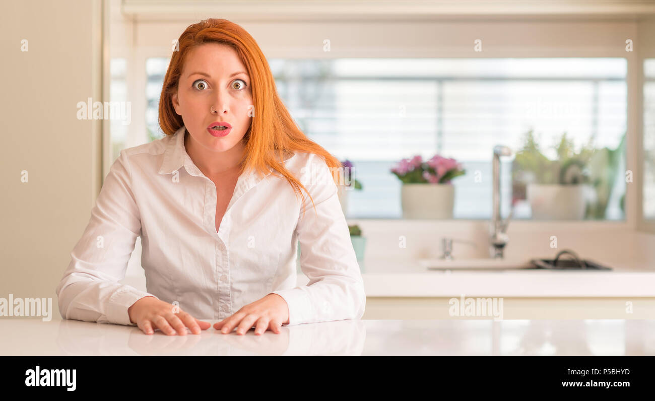 Redhead woman at kitchen afraid and shocked with surprise expression ...