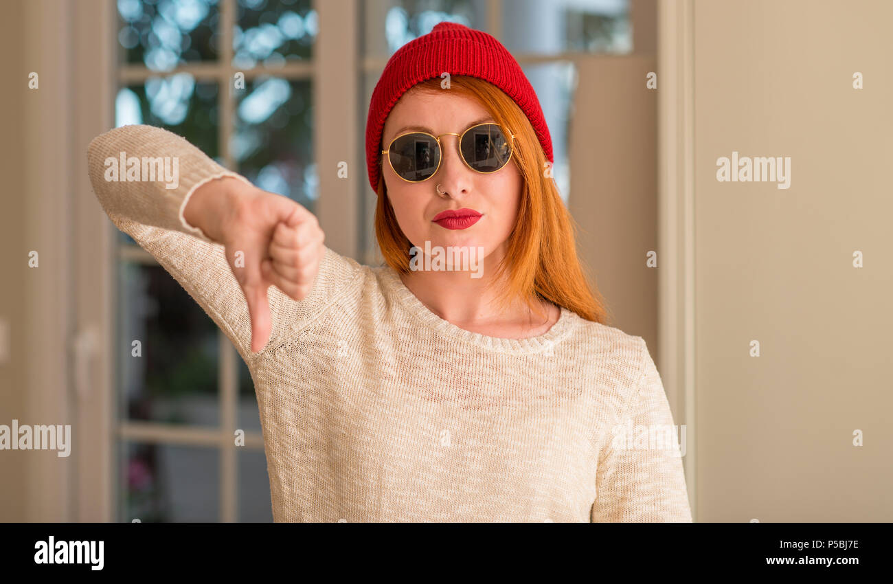 Stylish redhead woman wearing wool cap and sunglasses with angry face ...
