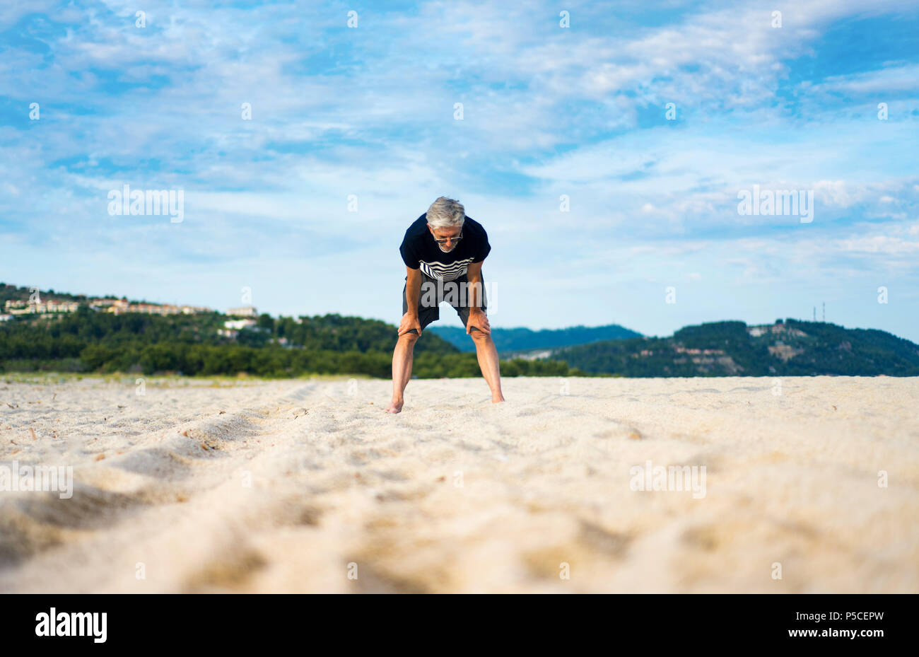 Tired senior taking rest during exercise on the beach, active lifestyle ...