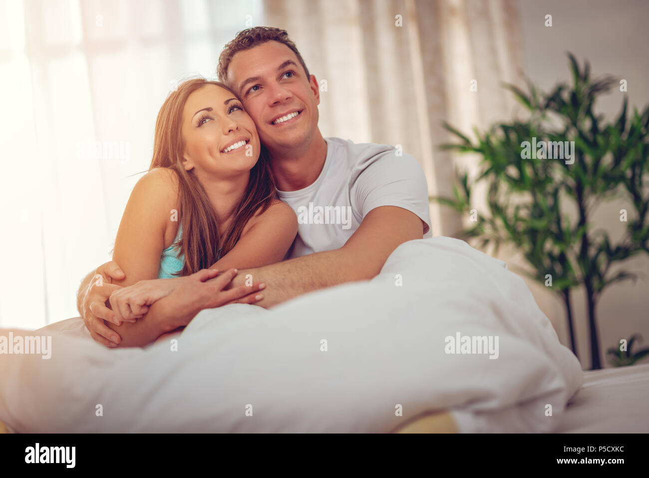 Beautiful young loving couple hugging and having lazy morning in bed ...