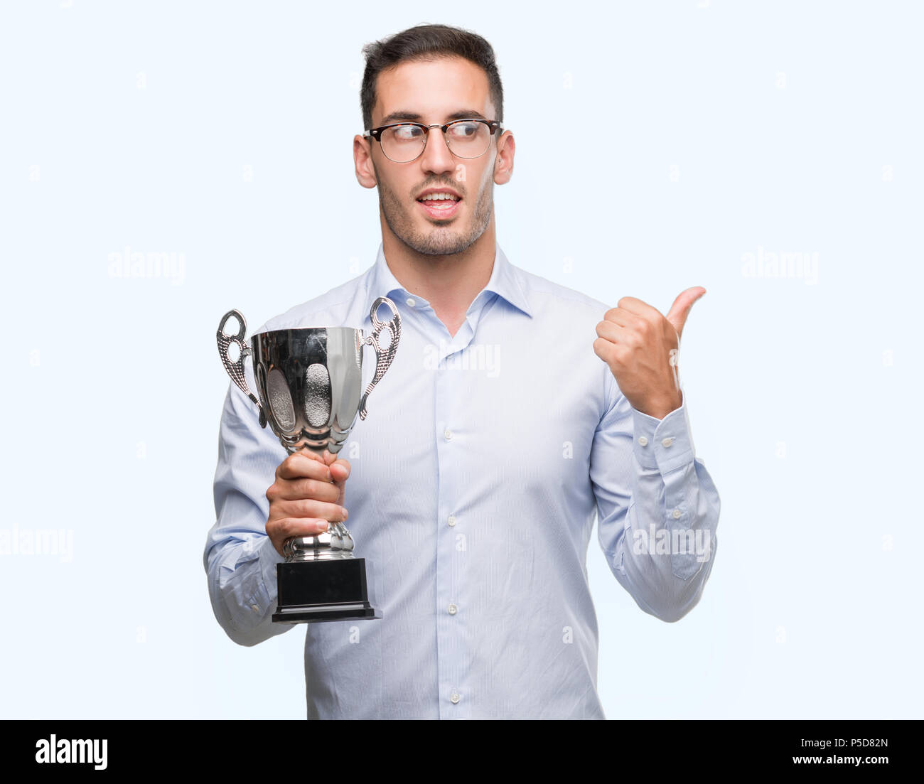 Handsome young man holding trophy pointing with hand and finger up with ...