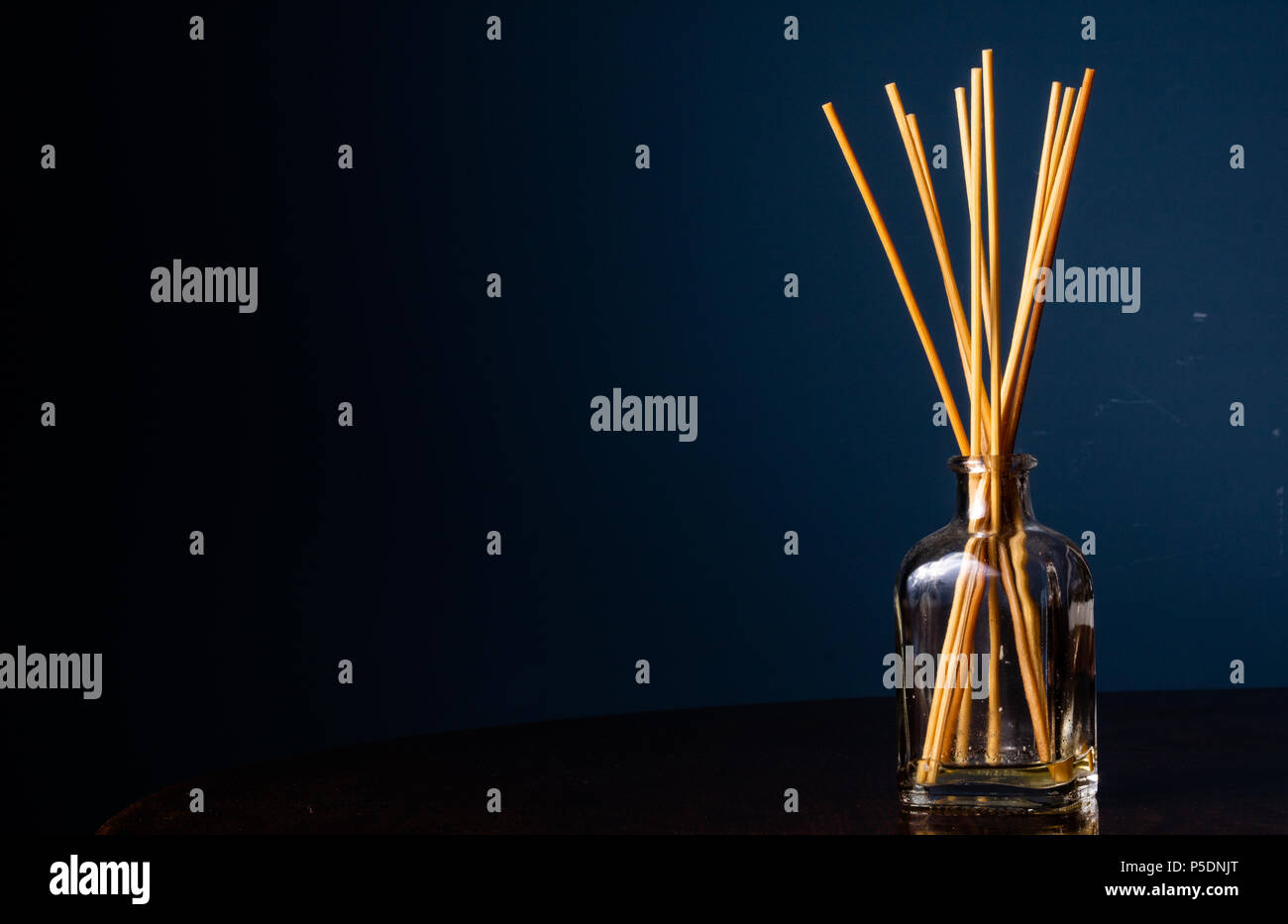 Reed diffusers in a small glass bottle on a table with a navy blue ...