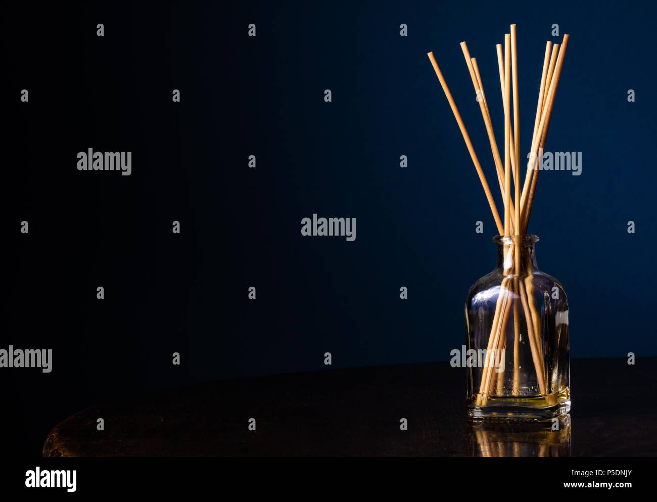 Reed diffusers in a small glass bottle on a table with a navy blue ...