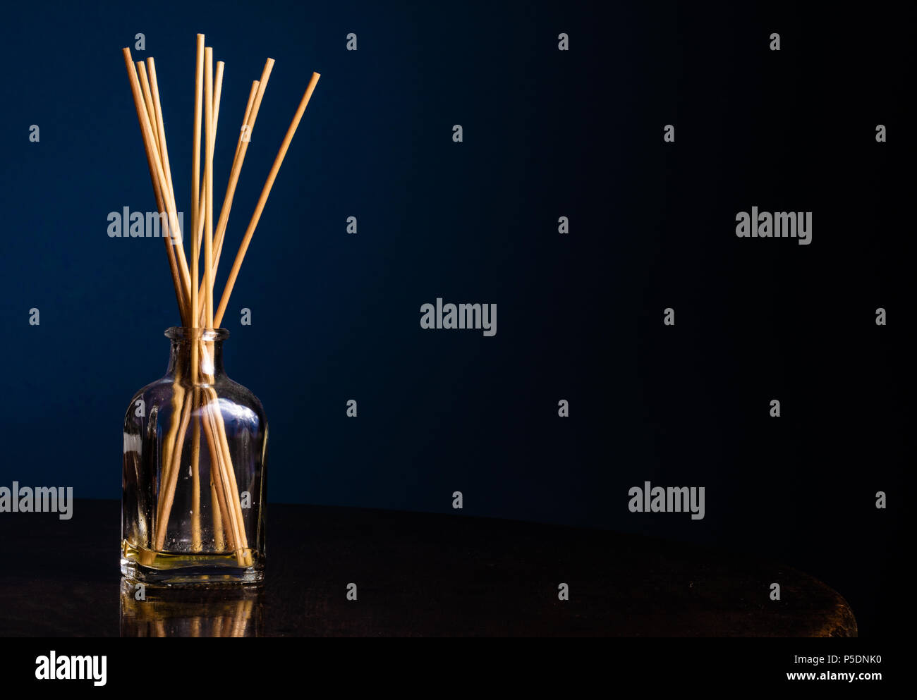Reed diffusers in a small glass bottle on a table with a navy blue ...