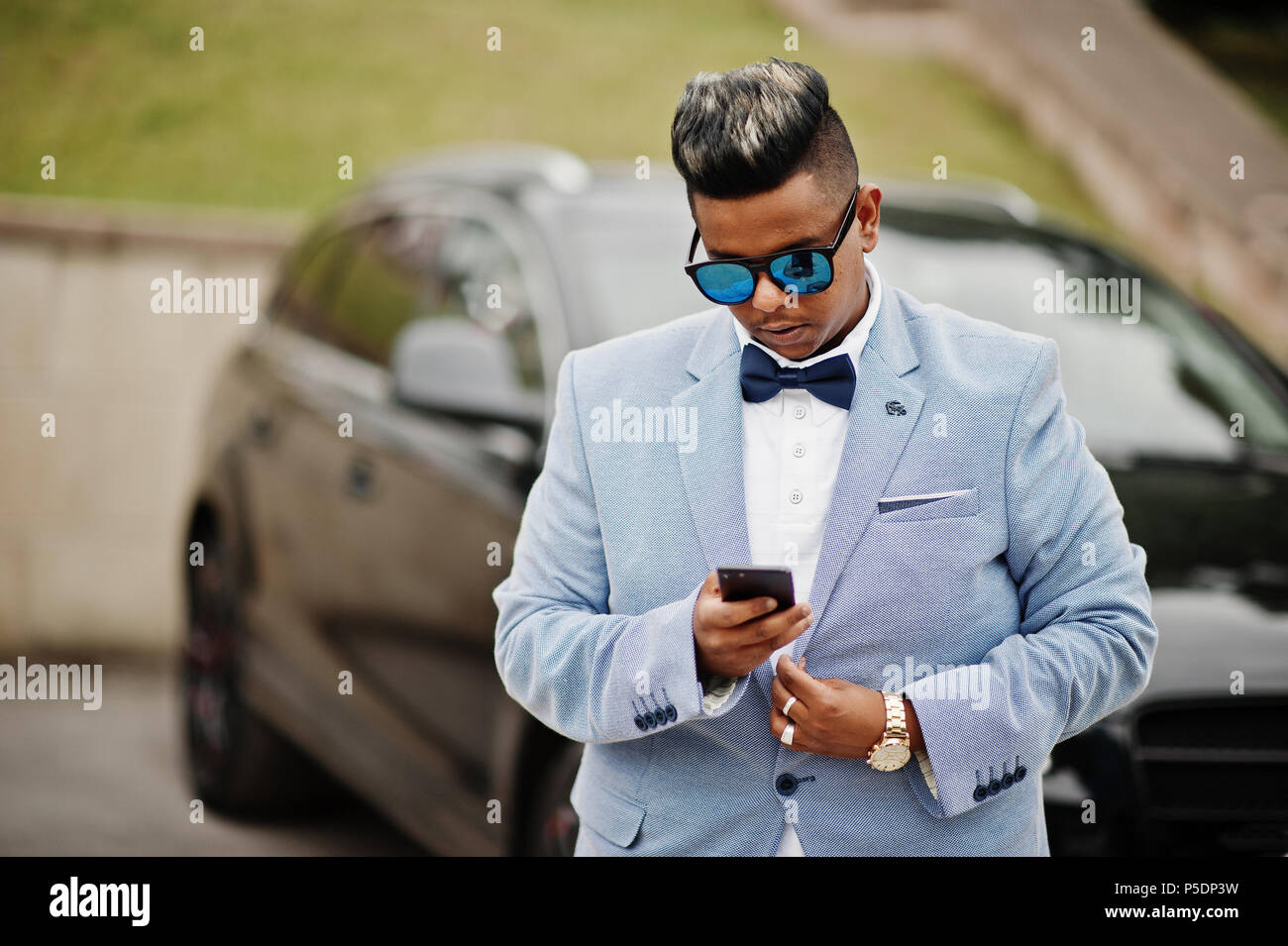 Stylish arabian man in jacket, bow tie and sunglasses against black suv ...