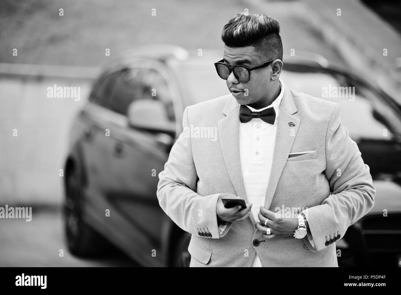 Stylish arabian man in jacket, bow tie and sunglasses against black suv ...