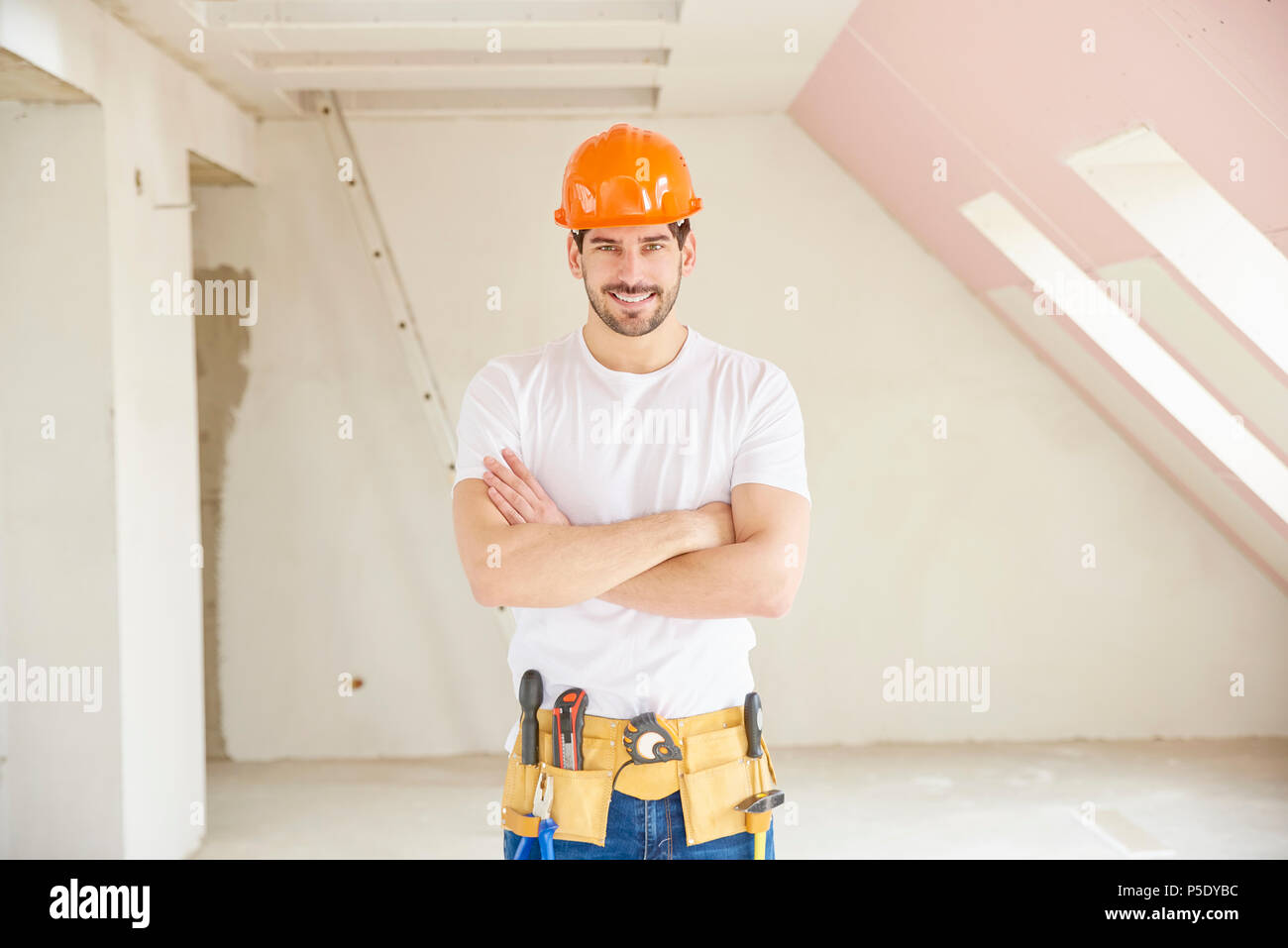 Handsome young handyman wearing hard hat and tool belt while standing ...