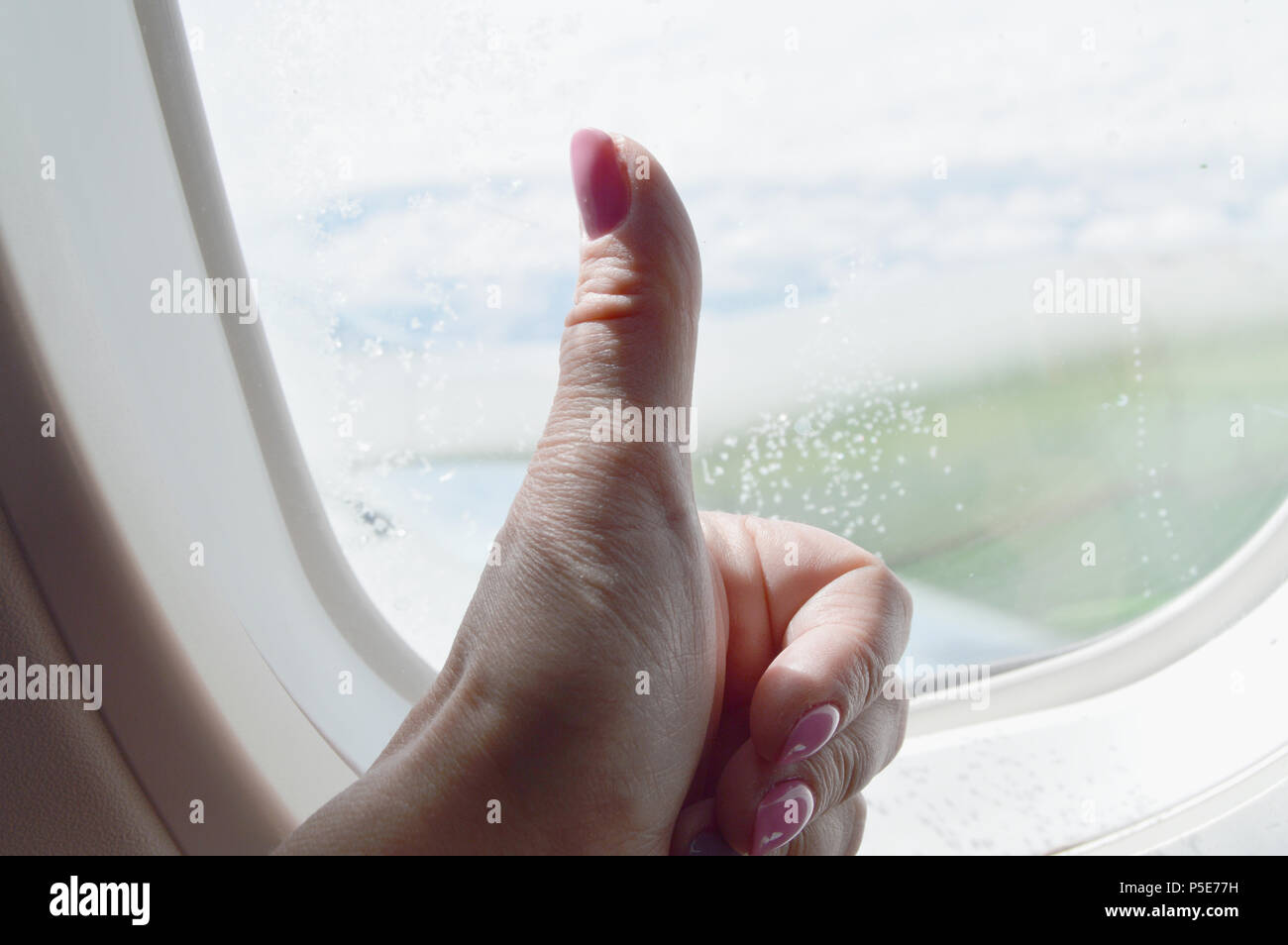 The female hand shows the thumb up, sitting in the plane at the window ...