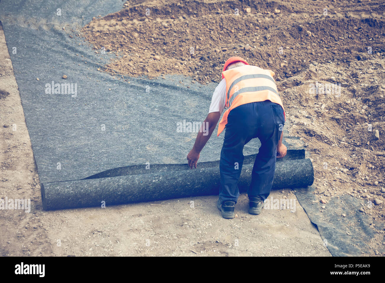 Worker laying geotextile in preparation for new building, used for ...