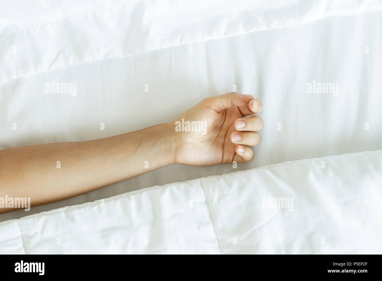 Close-up of lonely female hand lying on the white soft bed linen ...