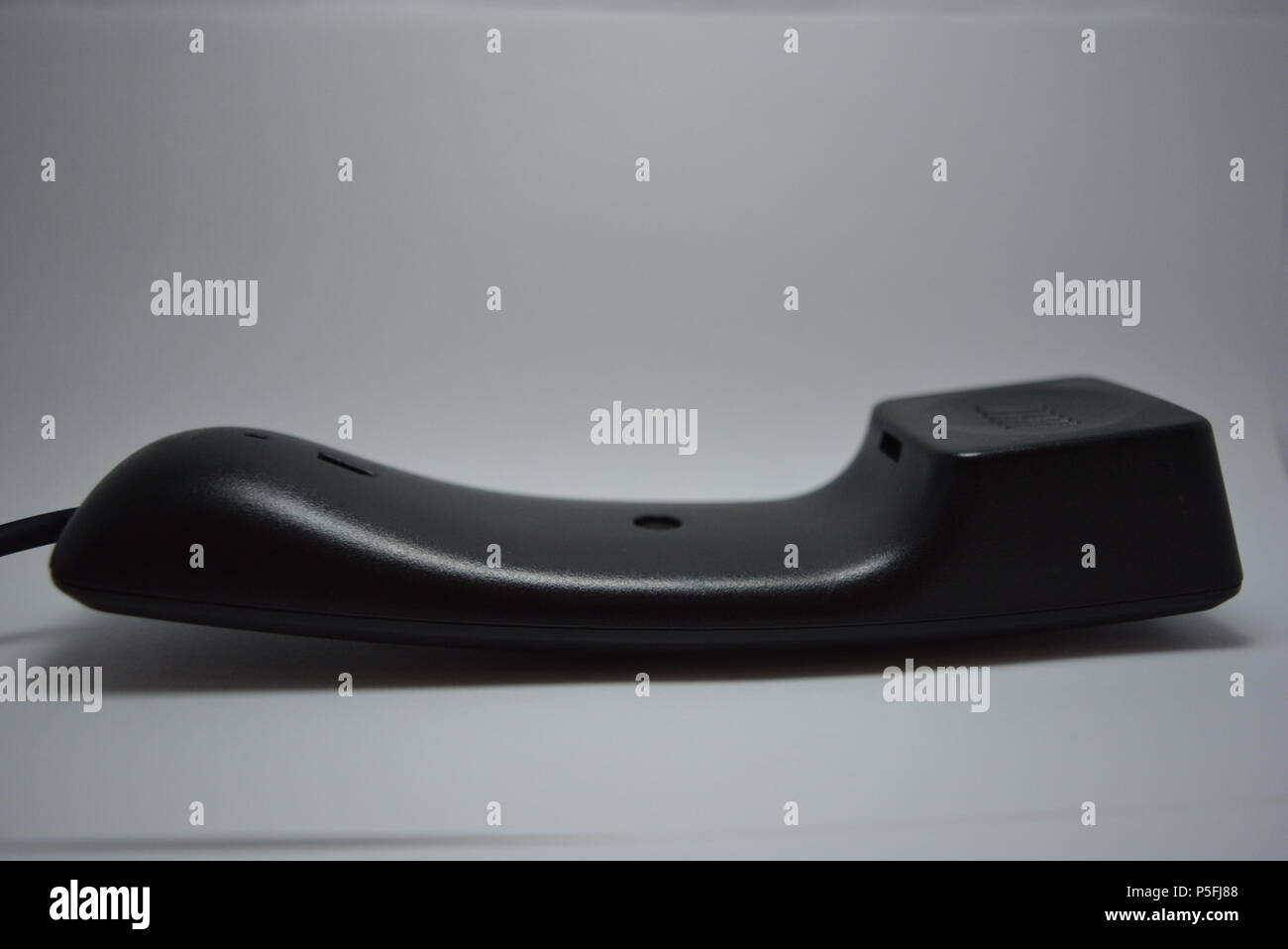 A black plastic handset from a landline phone without buttons is ...