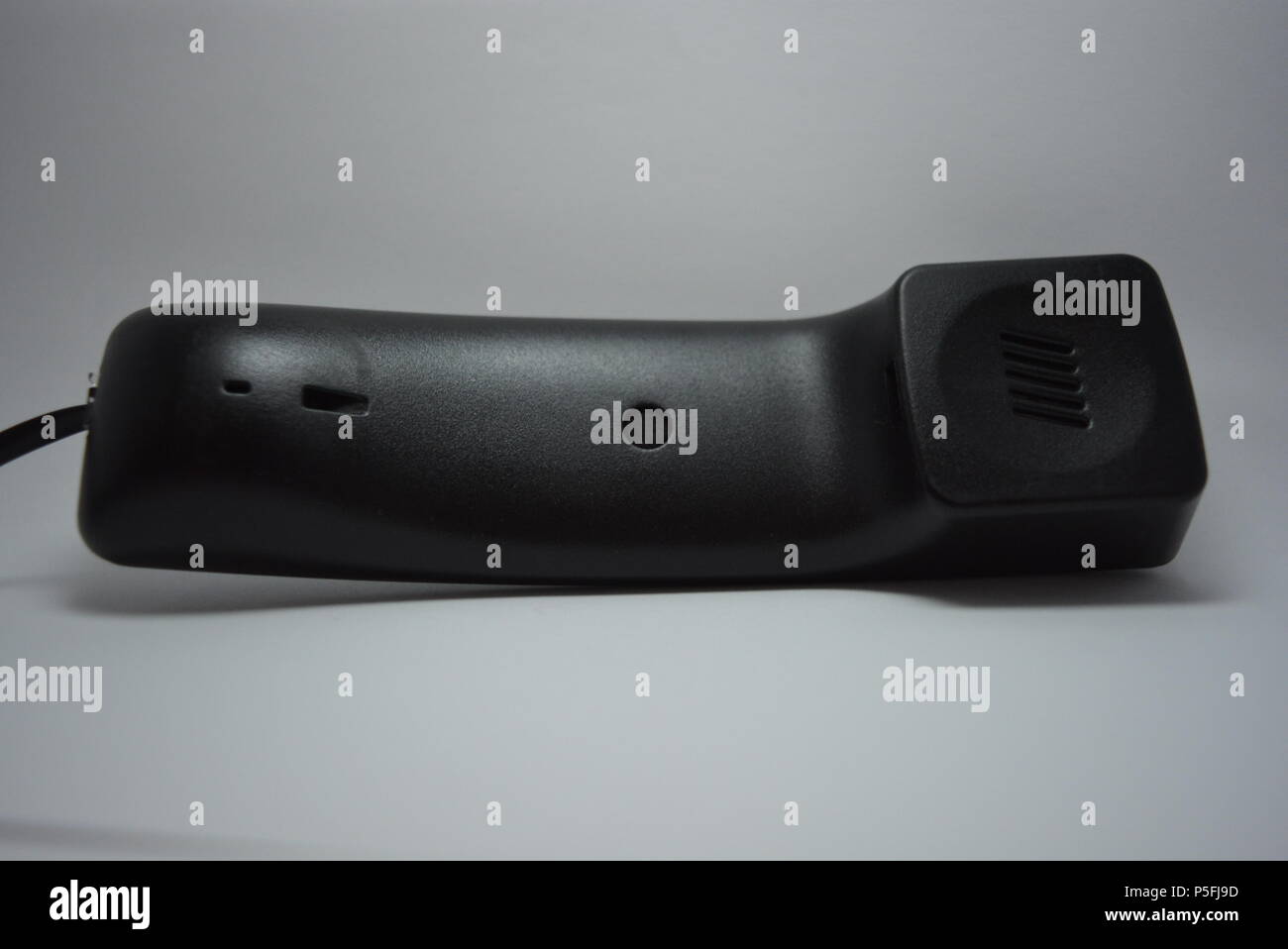 A black plastic handset from a landline phone without buttons is ...