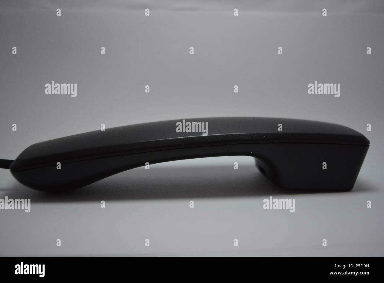 A black plastic handset from a landline phone without buttons is ...