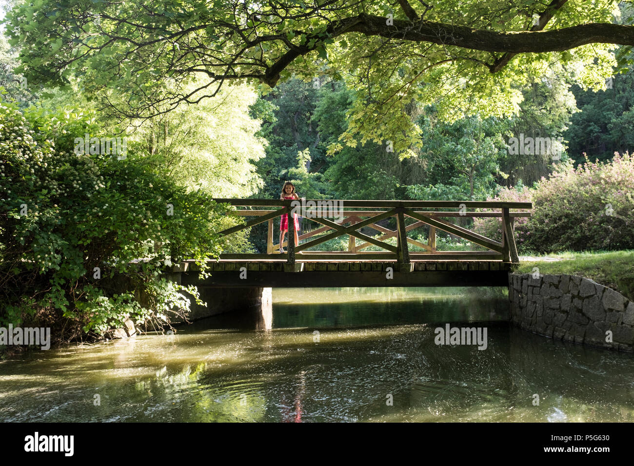 Girl looking over side of bridge at limpid green waters of river in ...