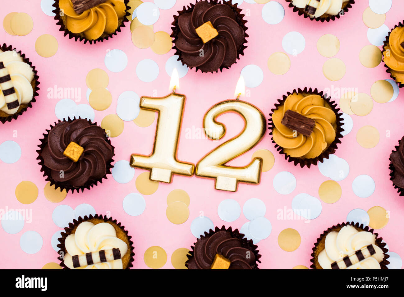 Number 12 gold candle with cupcakes against a pastel pink background ...