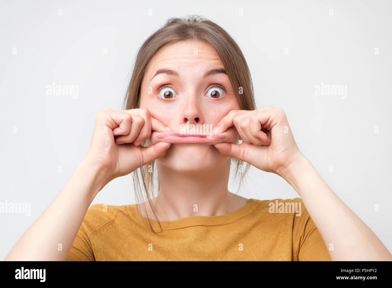 Caucasian young girl holding and stretching her lips. She wants to make ...