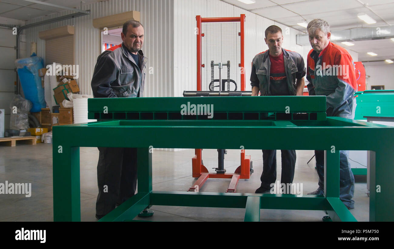 Male workers at manufacturing of CNC machines cleaning the workspace ...