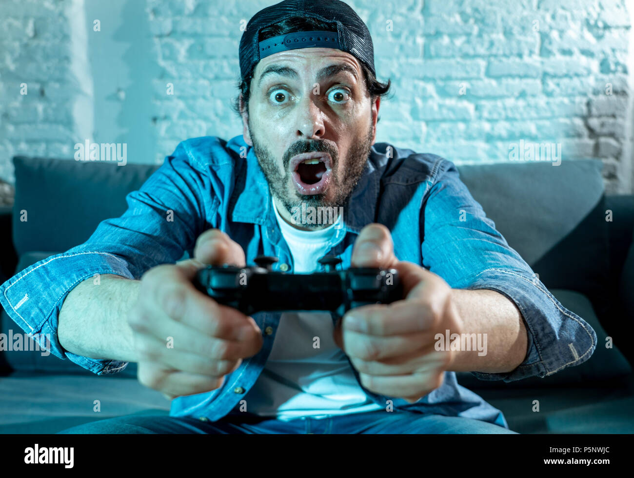 young excited latin man at home sitting in living room sofa playing ...
