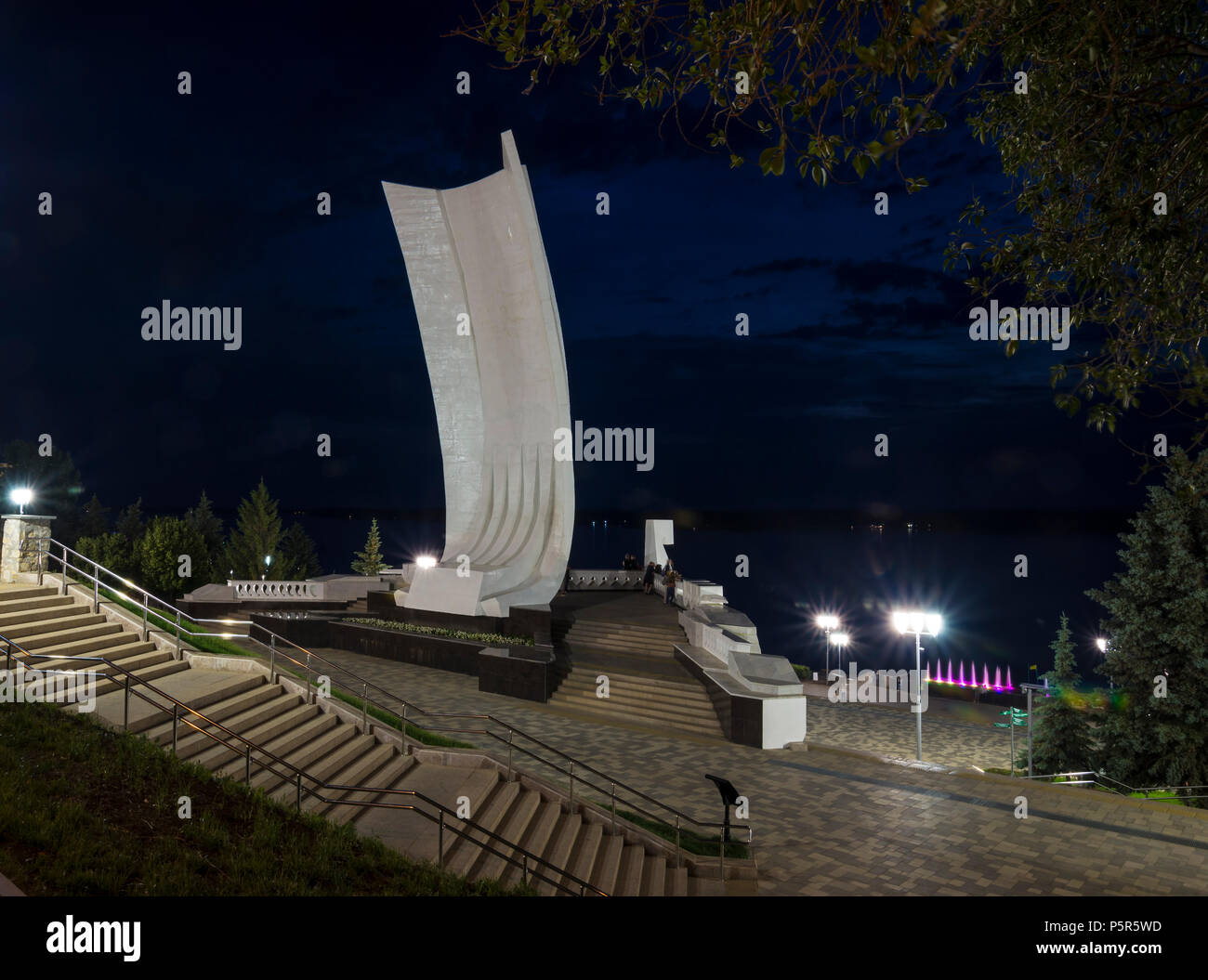 Monument in the form of a ship with a white sail on the Volga river embankment at night in ...