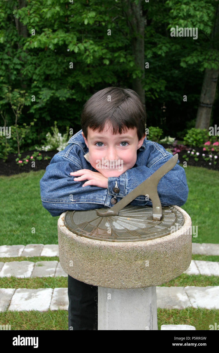 A young boy leans on a sundial outside in the sun and grins Stock Photo ...