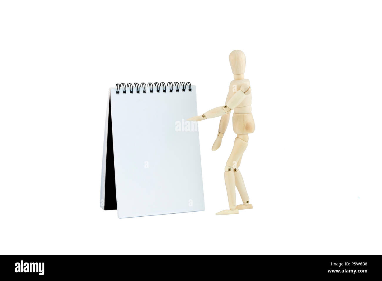 articulated wooden dummy indicating something in a notebook on white ...