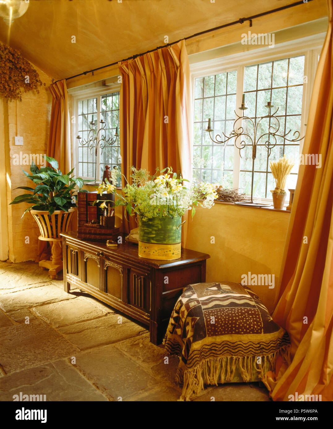 Rich ochre silk curtains on windows above antique chest with vase of ...